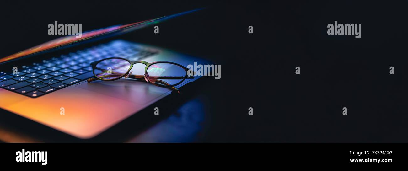 Glasses lie on the laptop, reflecting light from the screen in the dark ...