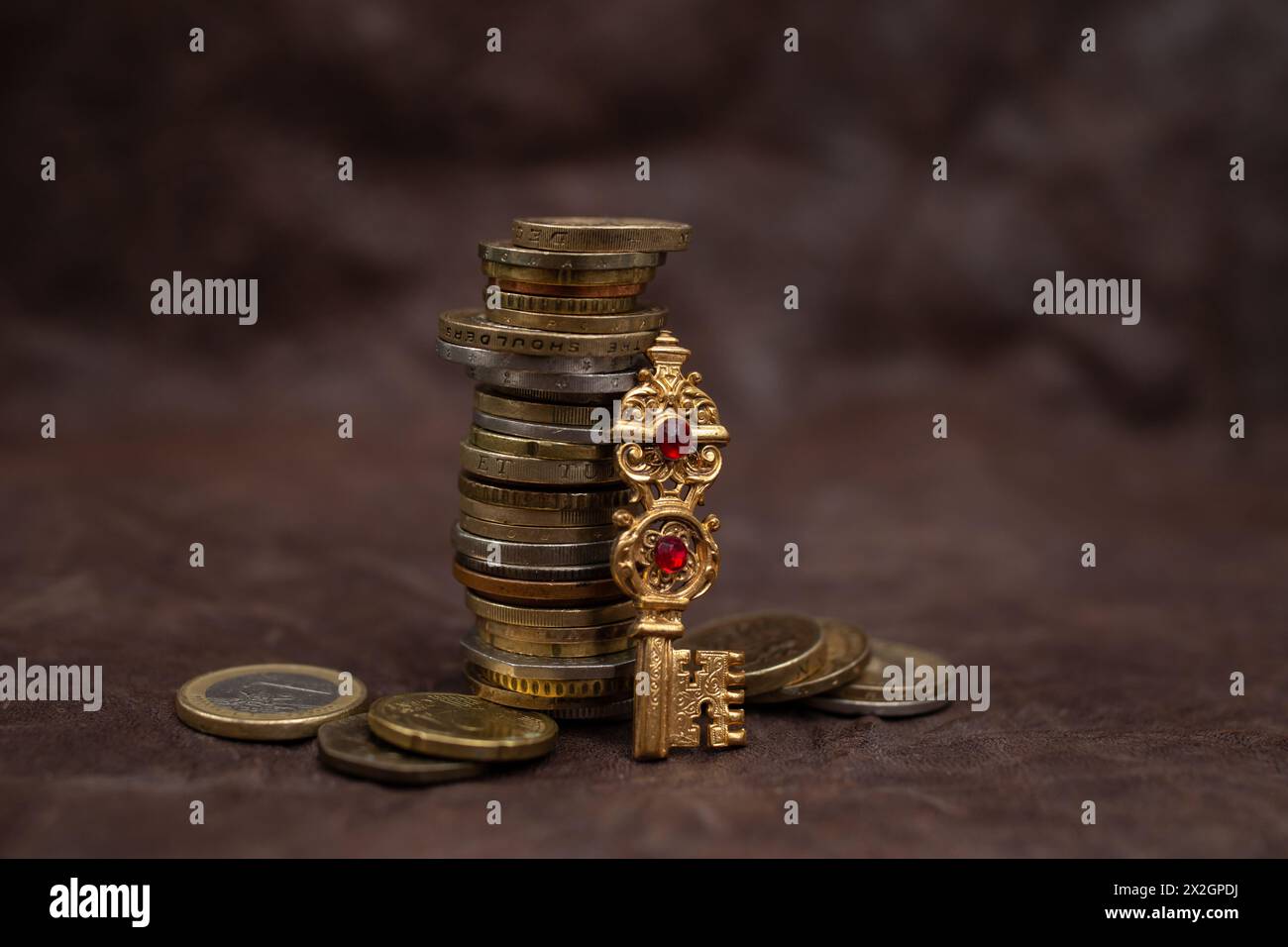Vintage golden key, with a stack of coins on brown leather desk ...