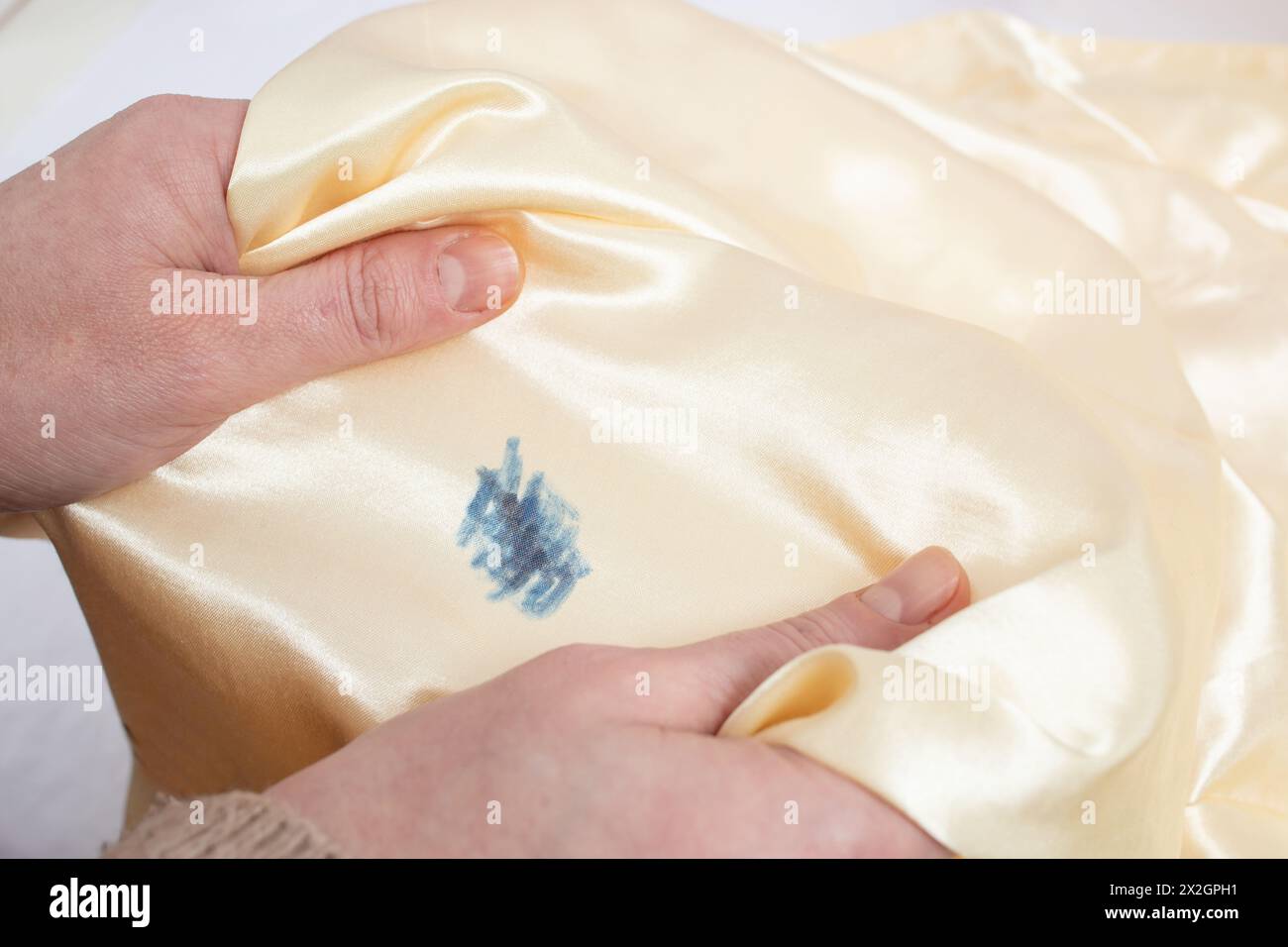 Woman hands stretching golden satin fabric with a blue ink stain, soft ...