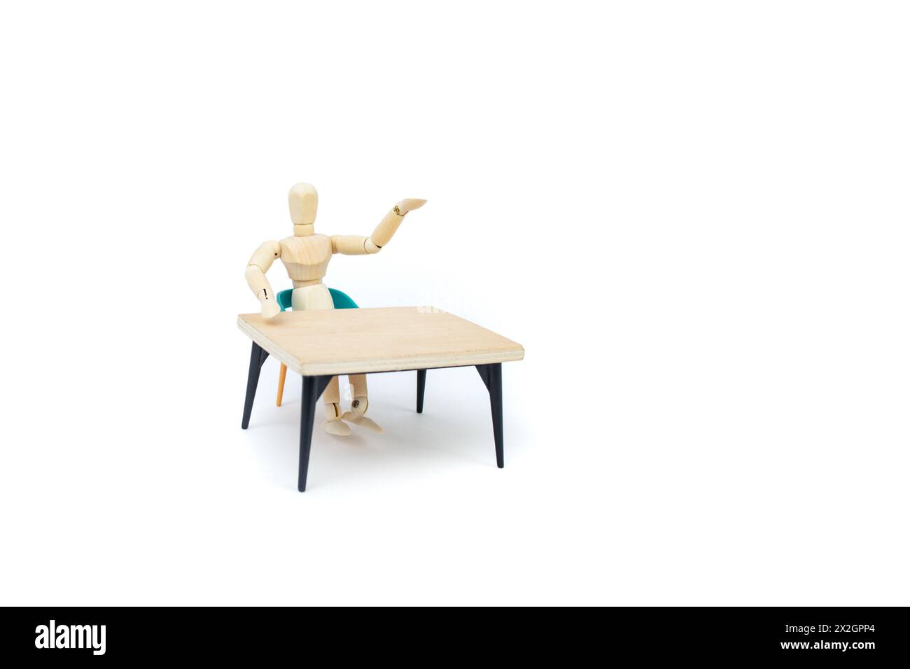 Wooden mannequin sitting on a chair at a empty table isolated on white ...