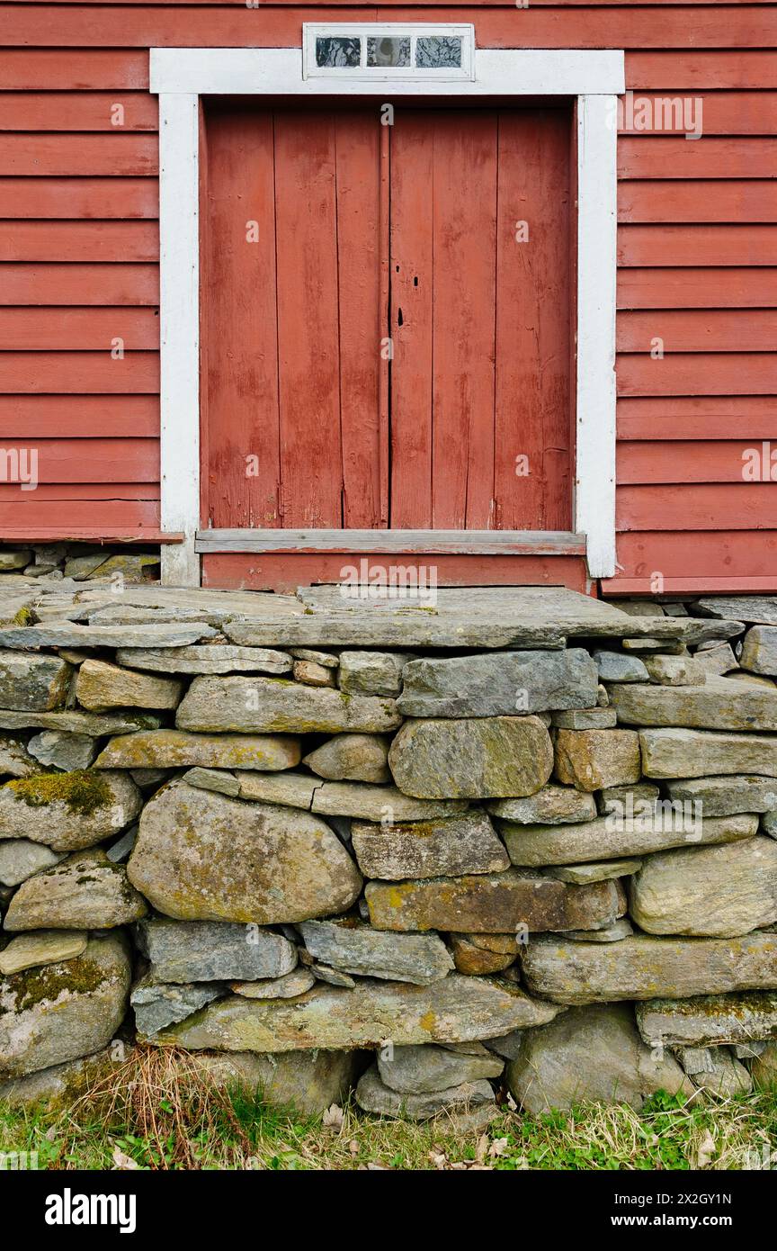 A weathered red barn door stands atop a rugged stone base, hinting at a ...
