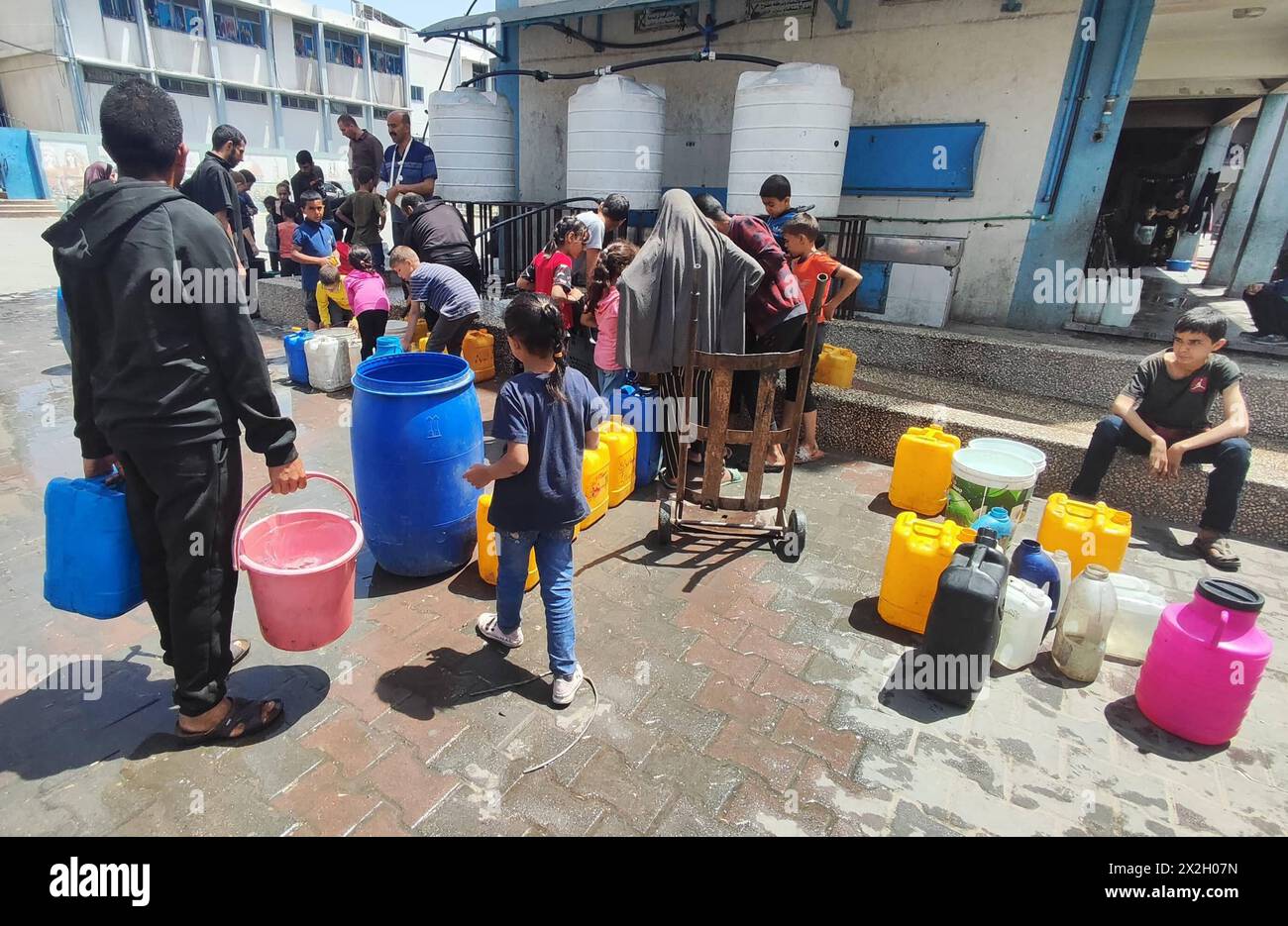 Displaced Palestinians line up to fill their containers with water in ...