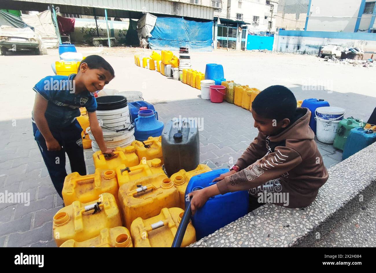 Displaced Palestinians line up to fill their containers with water in ...
