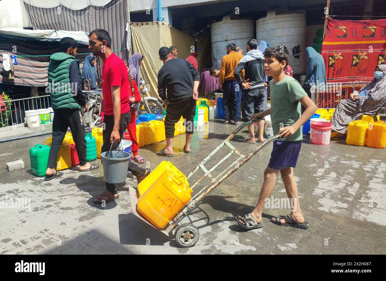 Displaced Palestinians line up to fill their containers with water in ...