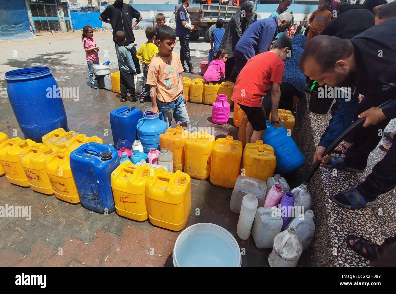 Displaced Palestinians line up to fill their containers with water in ...