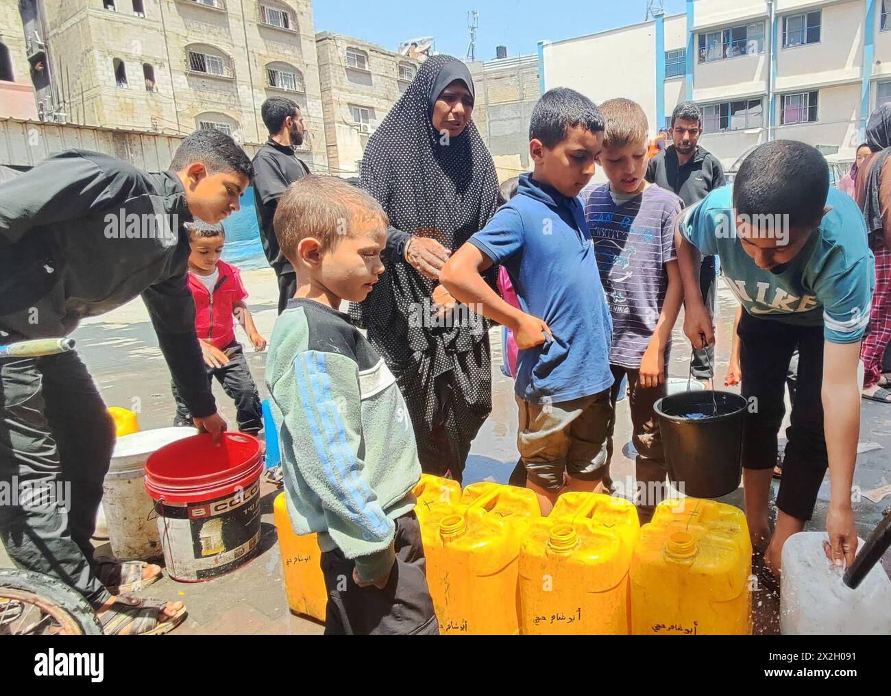 Displaced Palestinians line up to fill their containers with water in ...