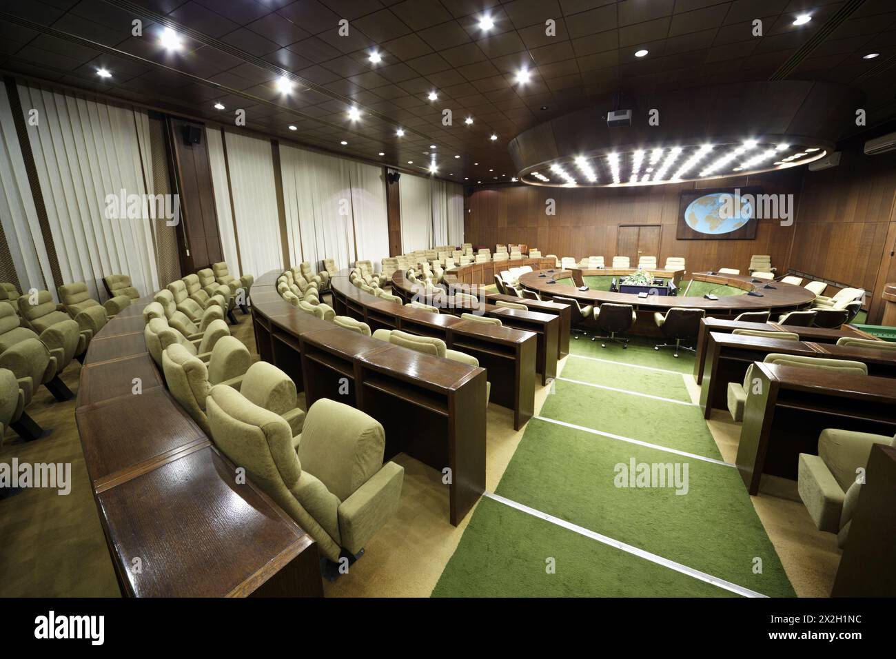 Auditorium round oak table and beige armchairs around it and rows of ...
