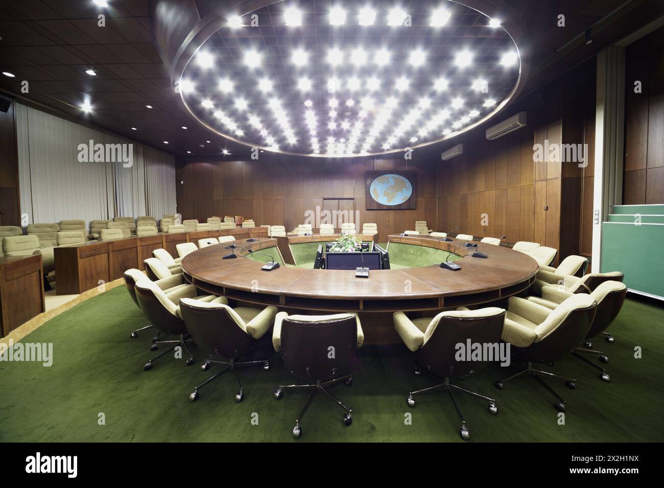Auditorium with round oak table, beige armchairs around it and flowers ...