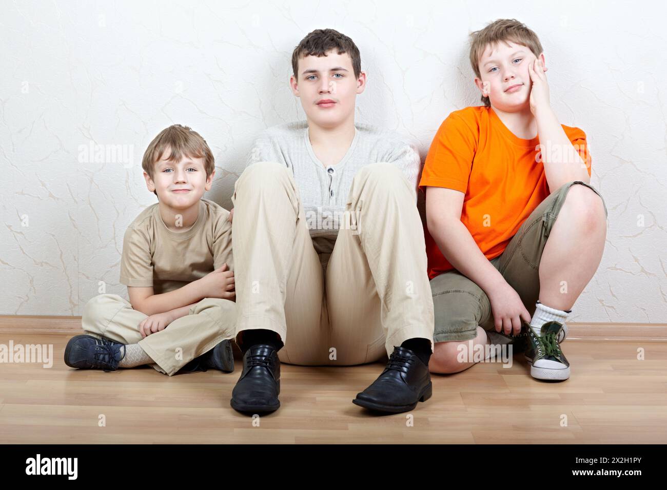 Three boys sit on the floor with their legs tucked up and with their ...