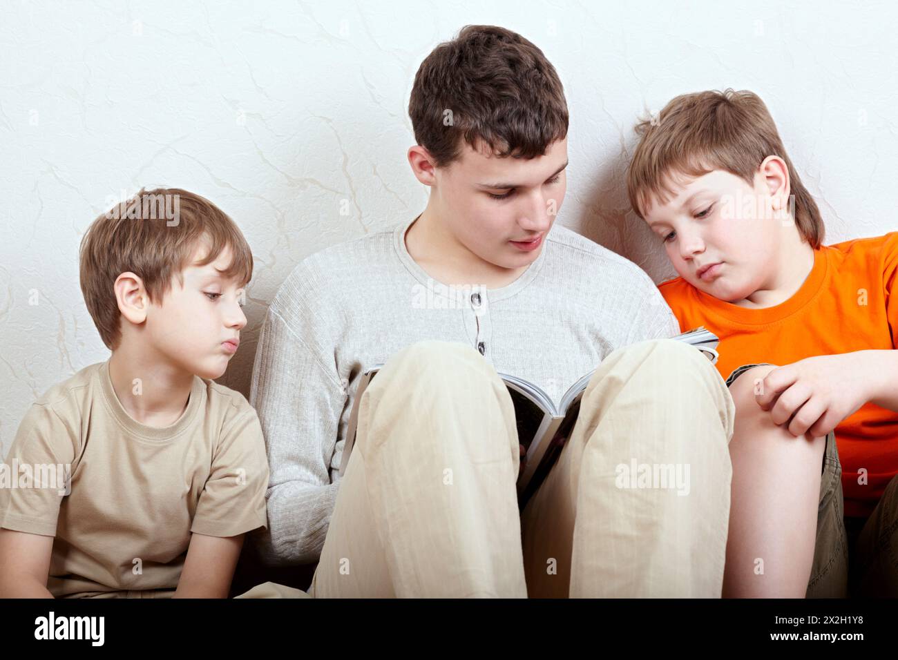 Three boys sit side by side with their backs to the wall and read ...