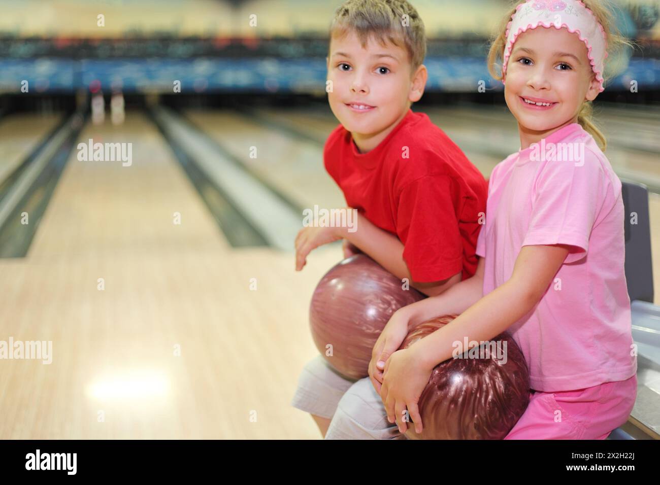 Happy brother and sister sit and hold balls in bowling club; bowling ...