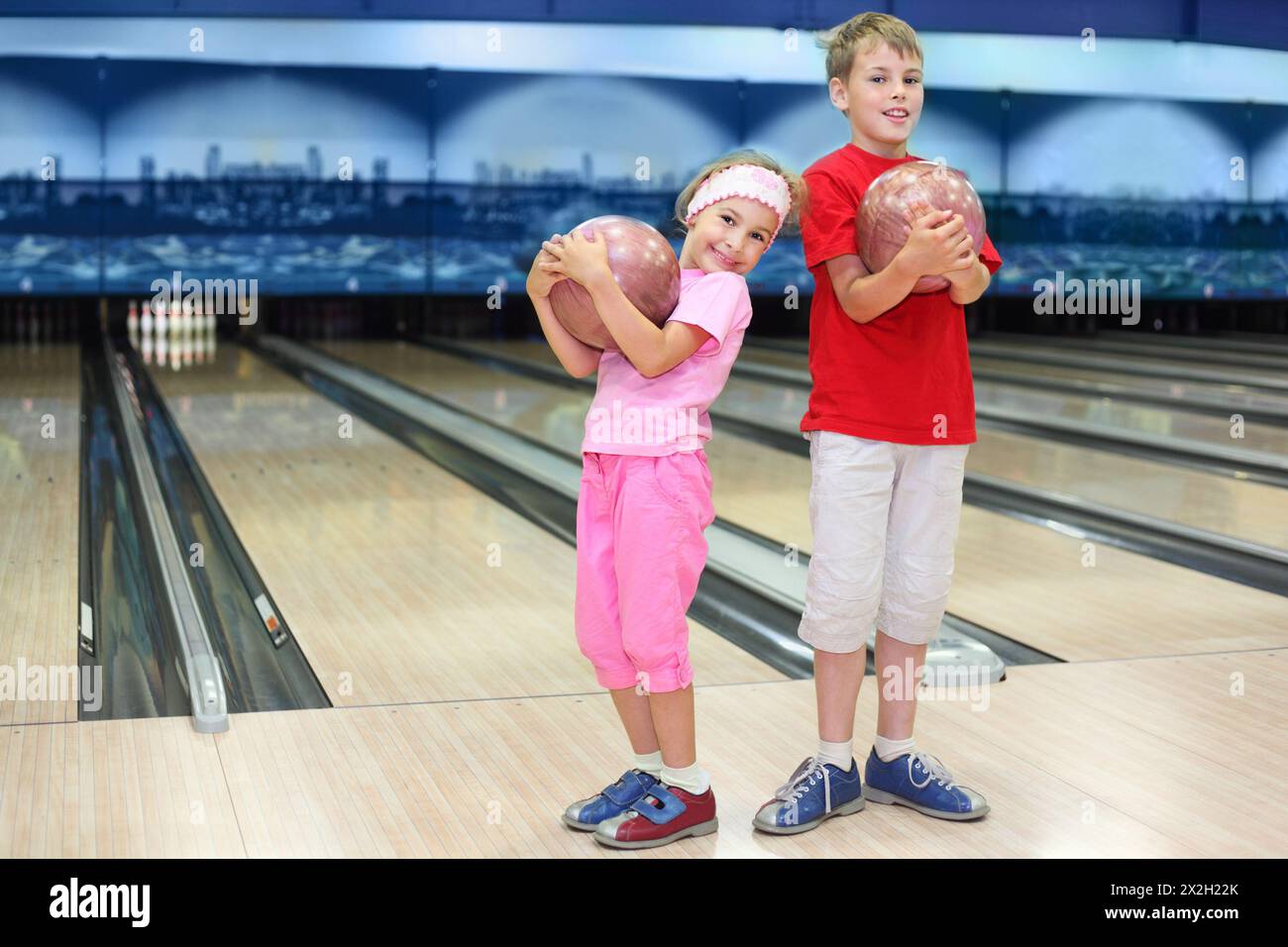 Smiling brother and sister hold balls in bowling club; bowling alleys ...