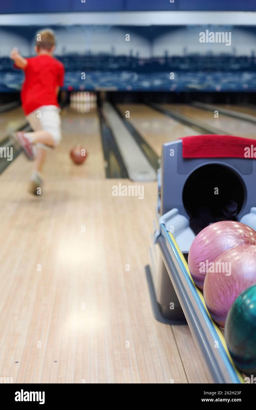 Boy throws ball in bowling; Focus on number of colorful balls; back of ...