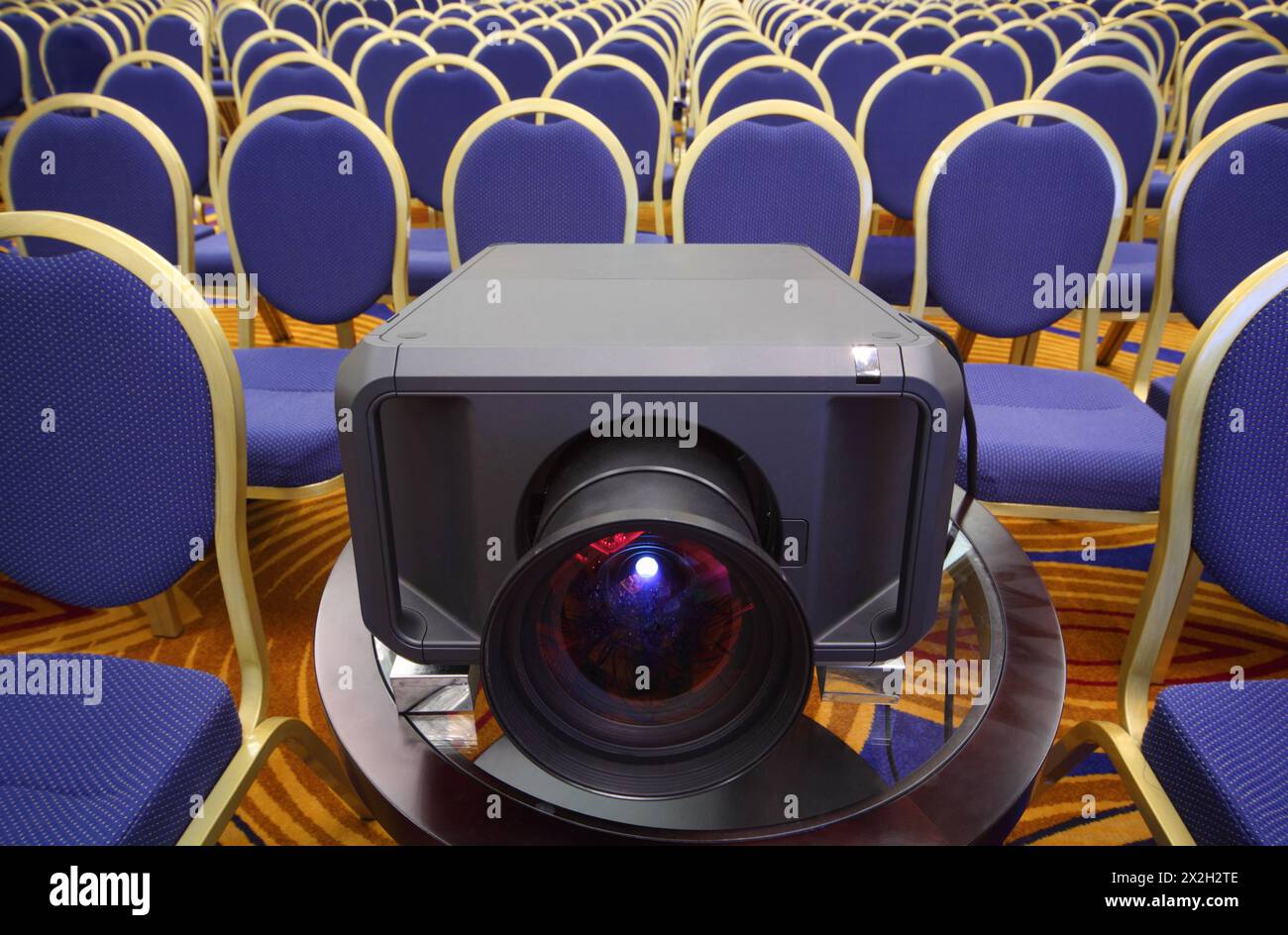 Black projector in center of rows of yellow-blue chairs in bright ...