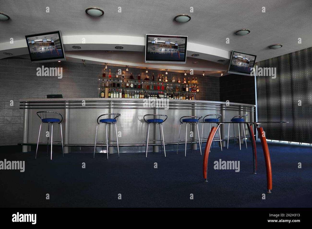 Bar interior with round counter, tv and stools; selves with many ...