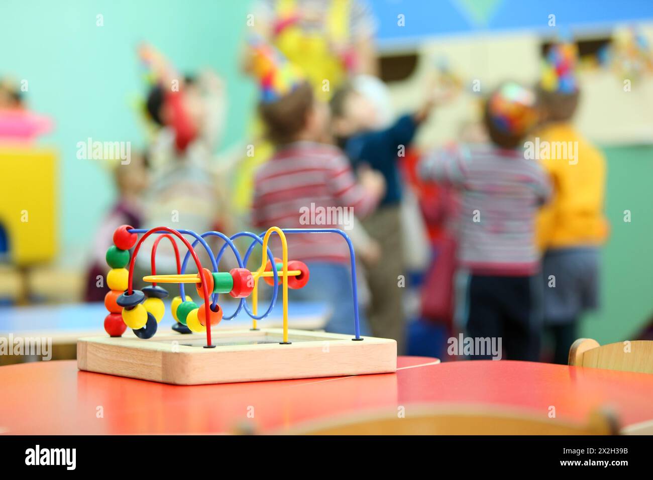 Colorful wooden toy stand at red table in kindergarten; children play ...