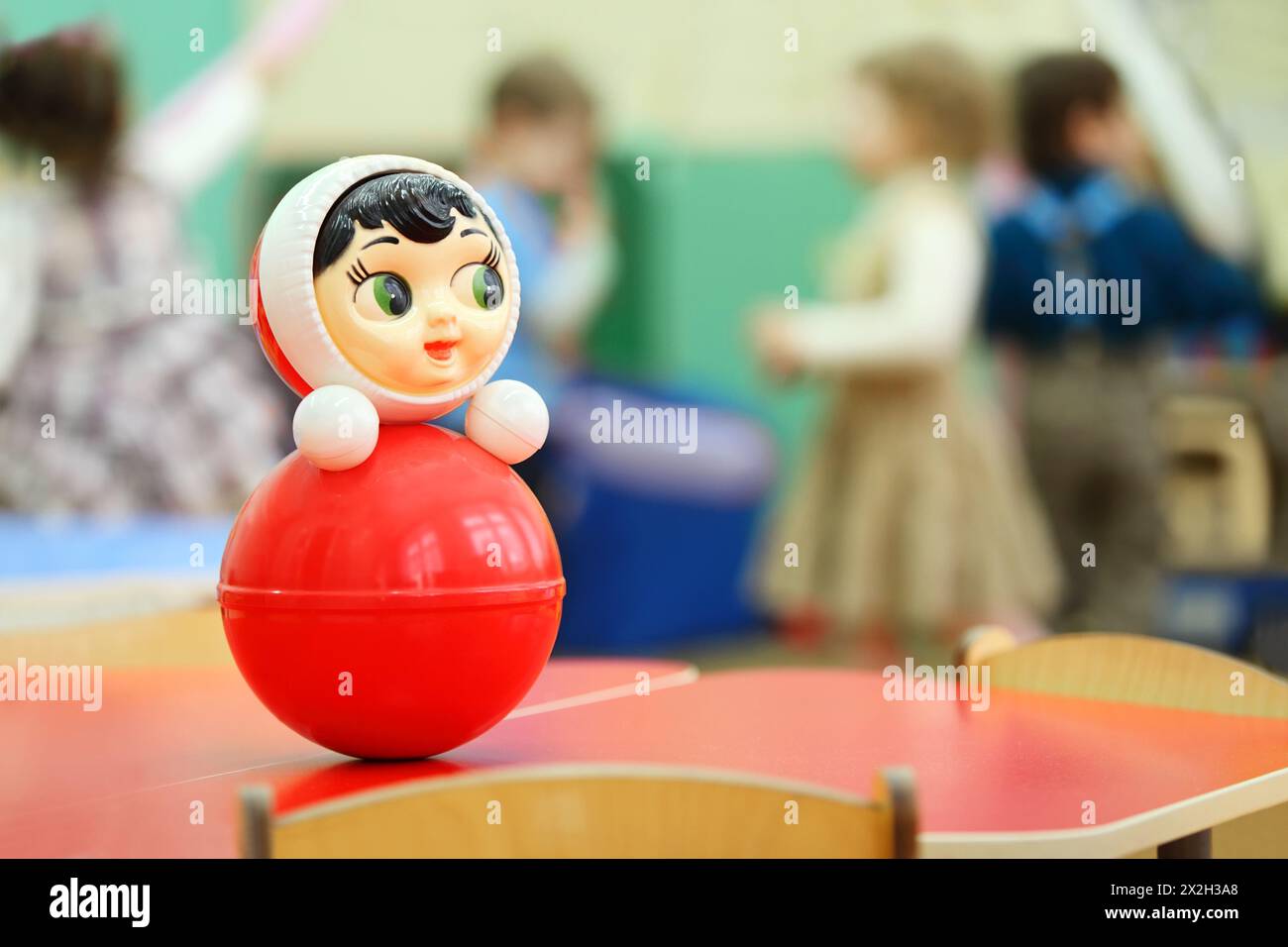 Bright red roly-poly toy stand at table in kindergarten; children play ...
