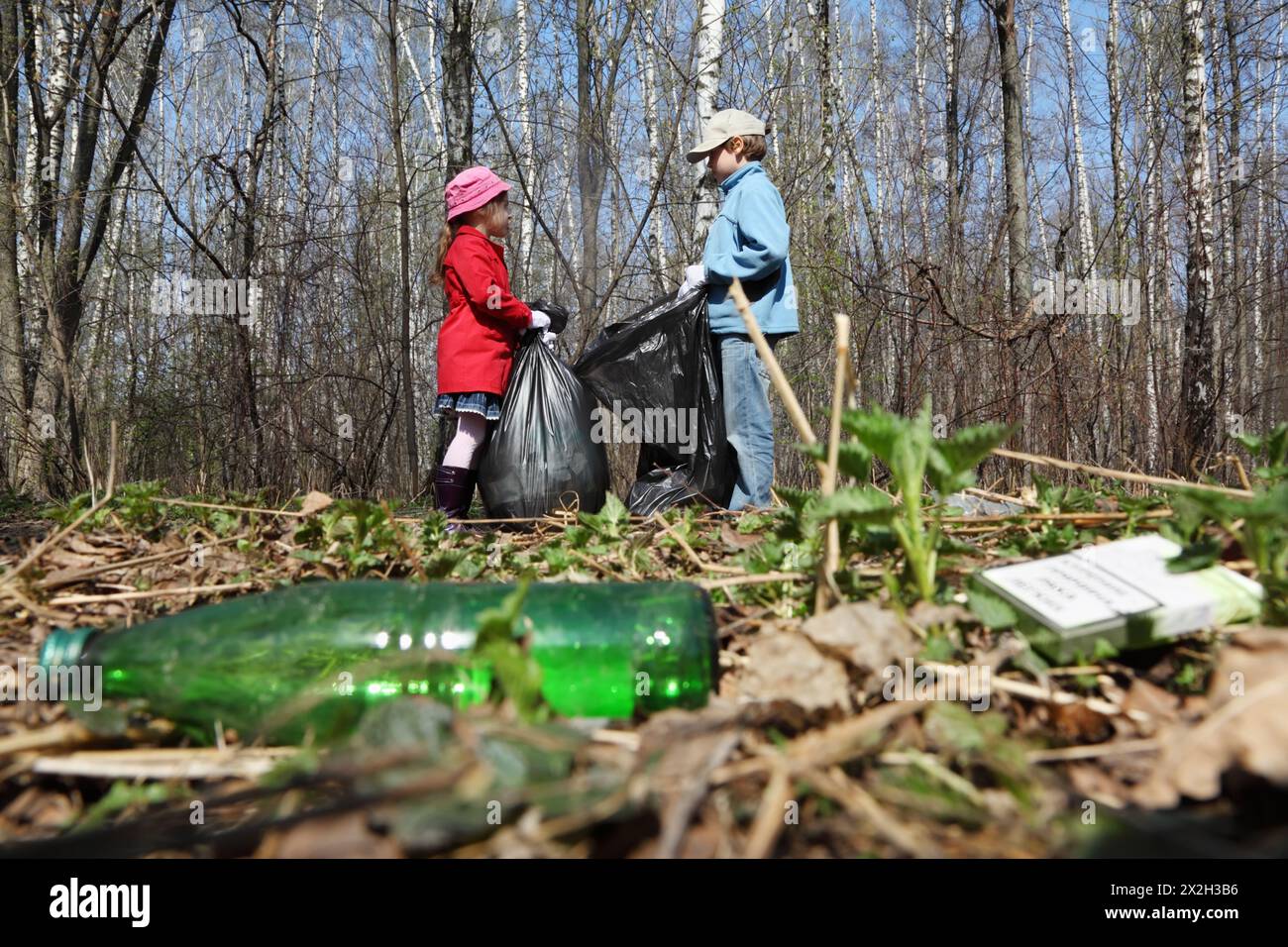 Brother and sister with black bags collect trash in park at spring ...