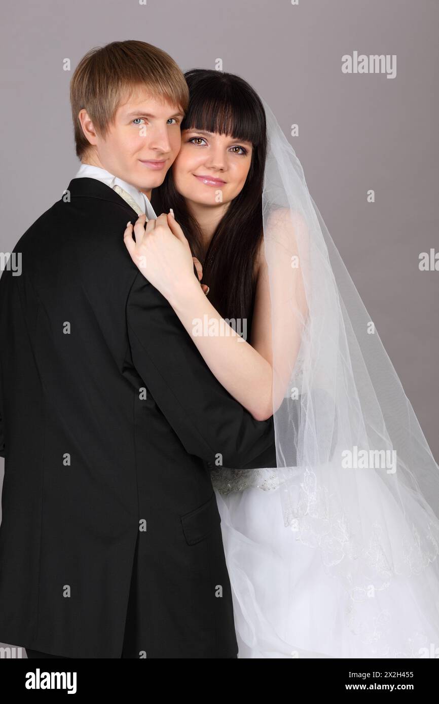 Happy young groom and bride embrace in studio on gray background; man ...