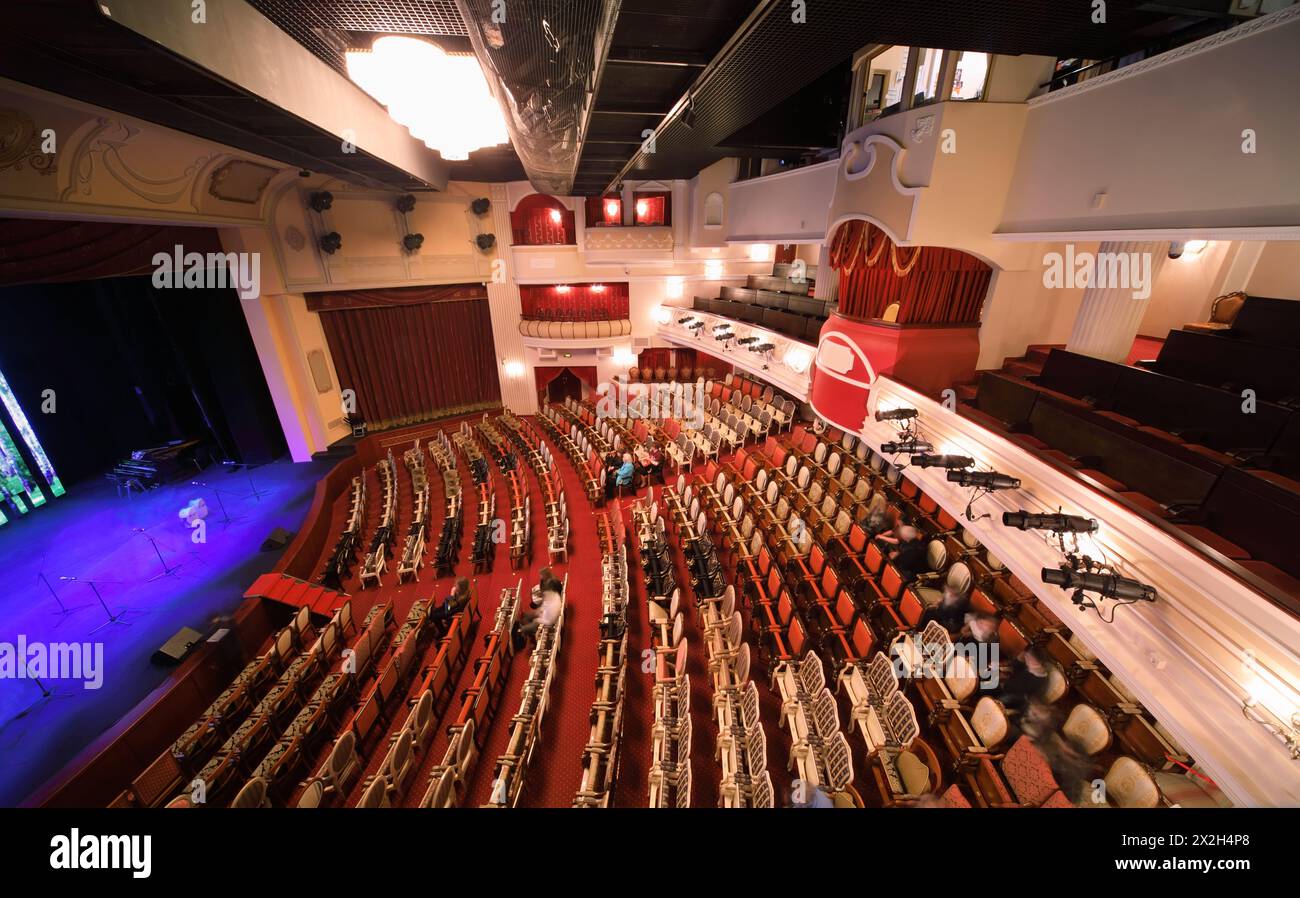 People sit down before concert in empty concert hall; blue stage and ...