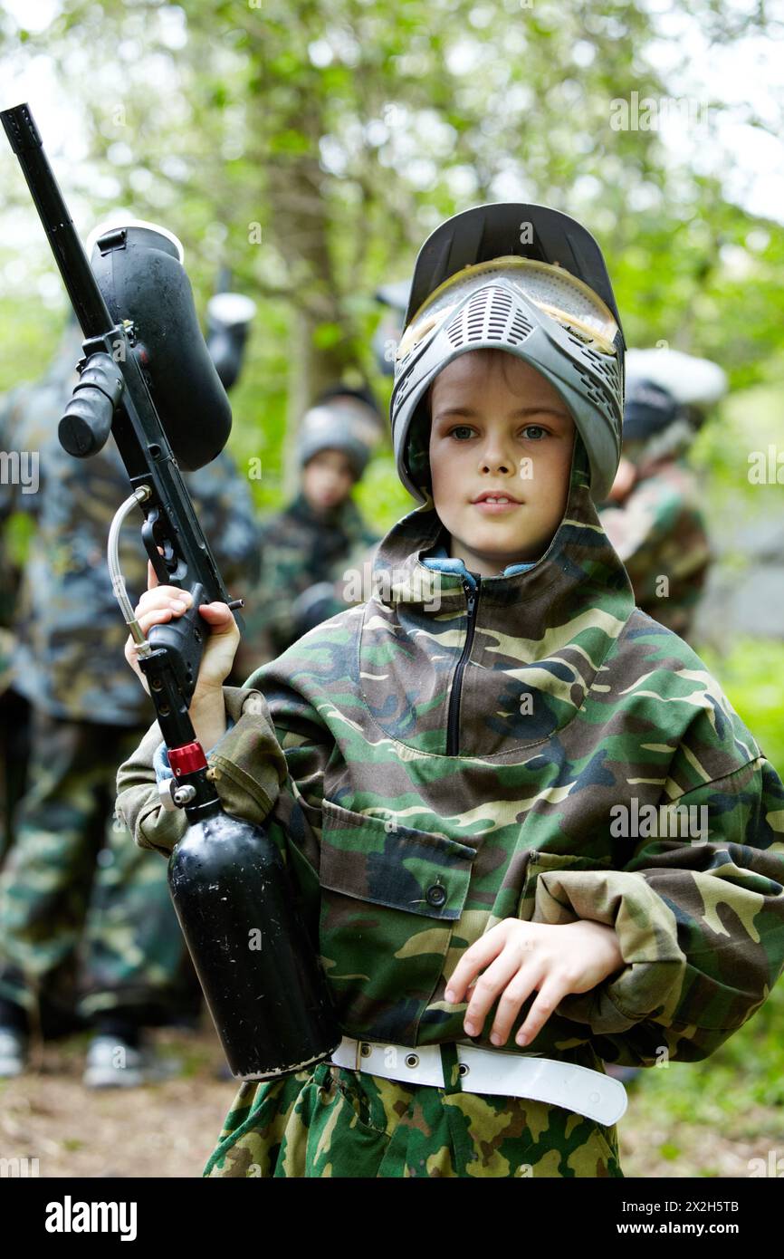 Boy in the camouflage suit holds a paintball gun barrel up , standing ...