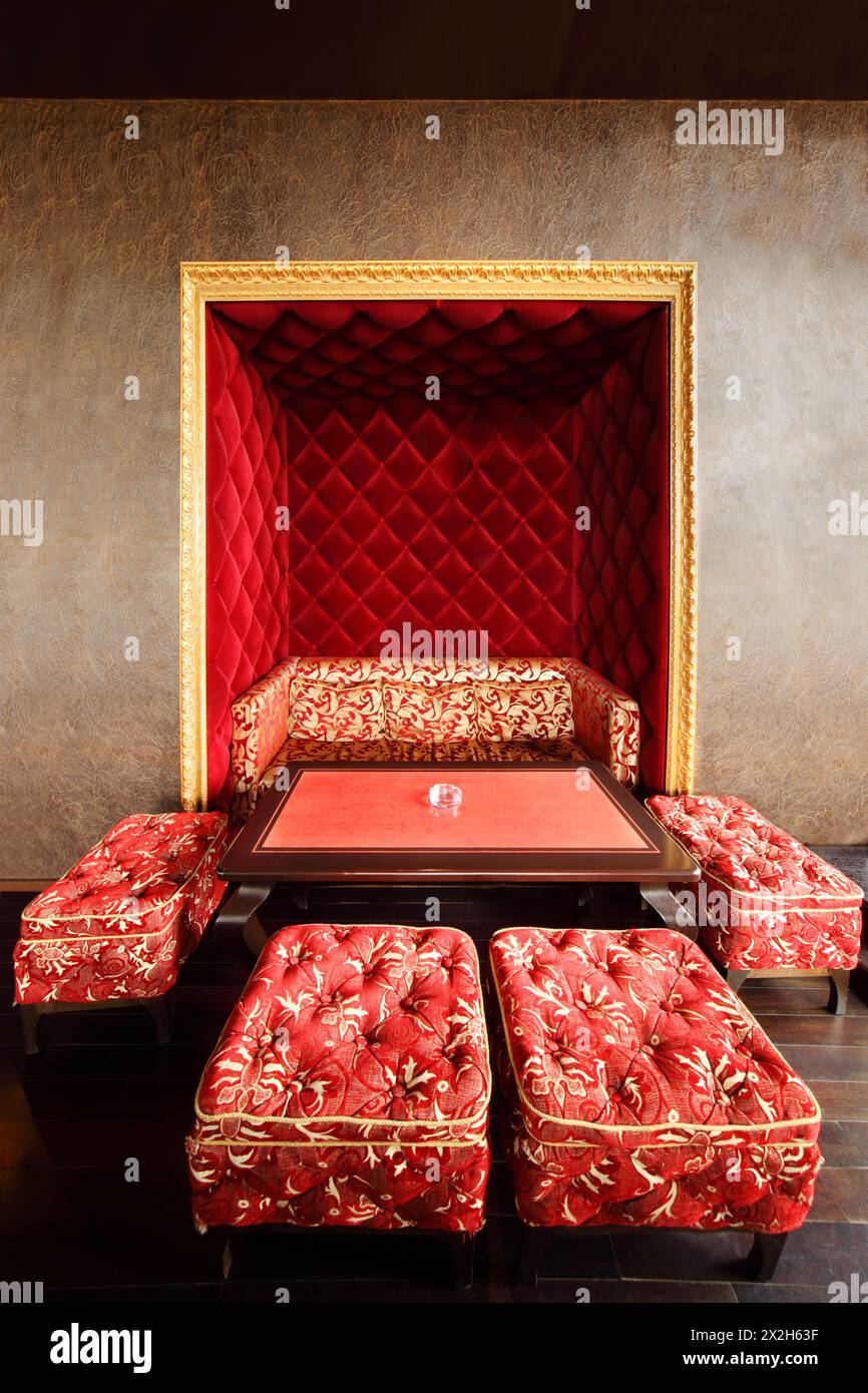 Beautiful red couch in niche, table and stools in empty stylish ...