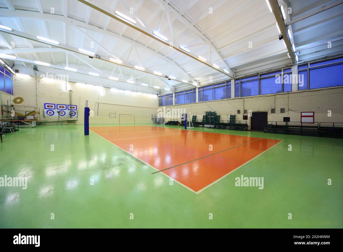 Inside lighted school gym hall with green-orange floor and volleyball ...