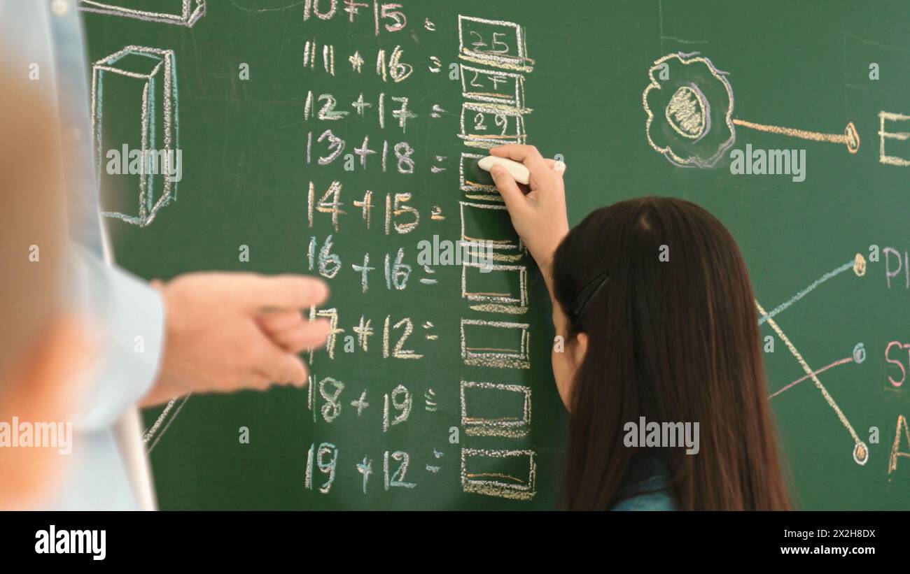 Young asian girl writing math formula at blackboard while standing at ...