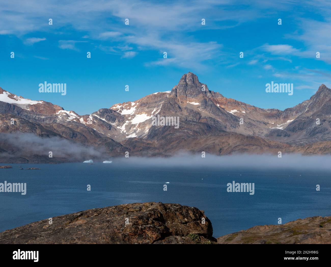 View of a prominent mountain in the bay of Tasiilaq with a strip of fog ...