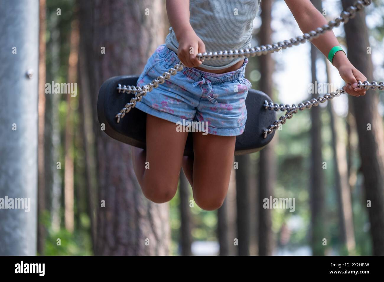 Child on a swing, mid,swing, legs lifted, wearing patterned blue shorts ...