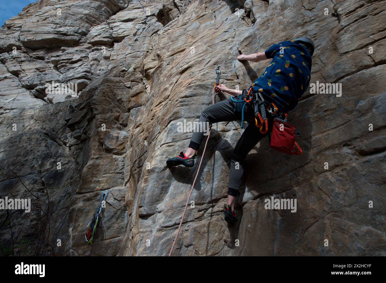 Back of male climber climbing up rock face showing foot and hand ...