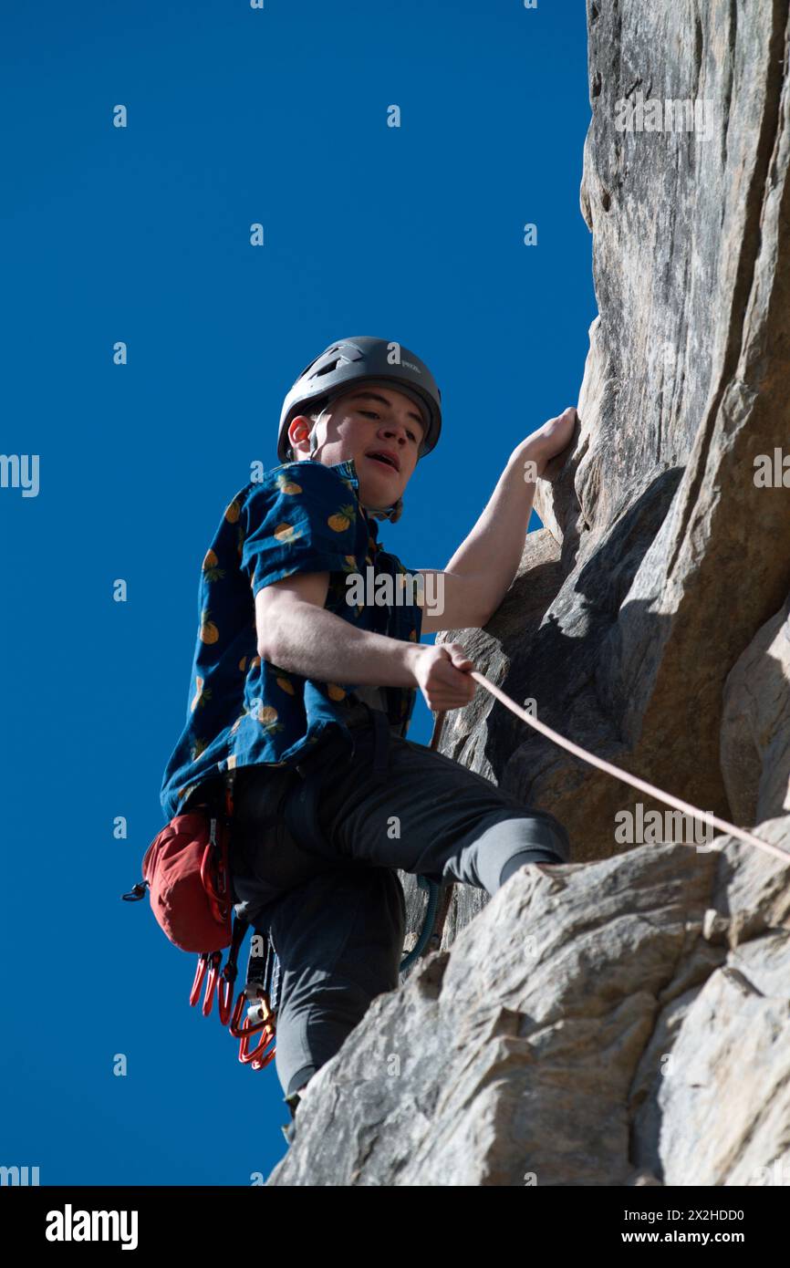 Male climber at top of rock face looking down and pulling on rope Stock ...