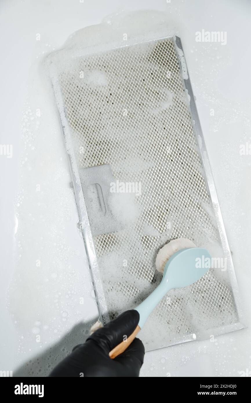 Hand in black glove cleaning mesh filter of cooker hood with brush and ...