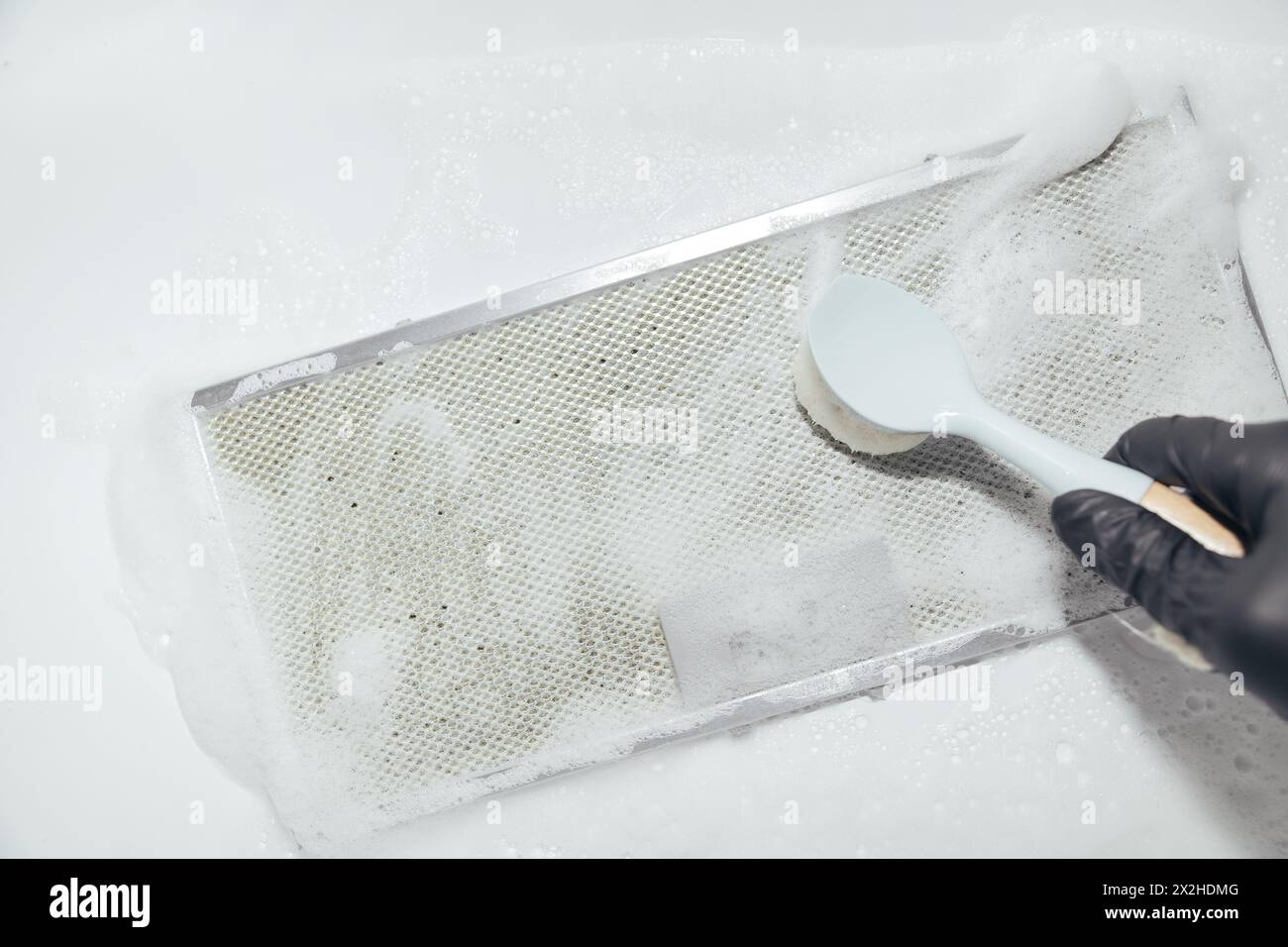 Hand in black glove cleaning mesh filter of cooker hood with brush and ...