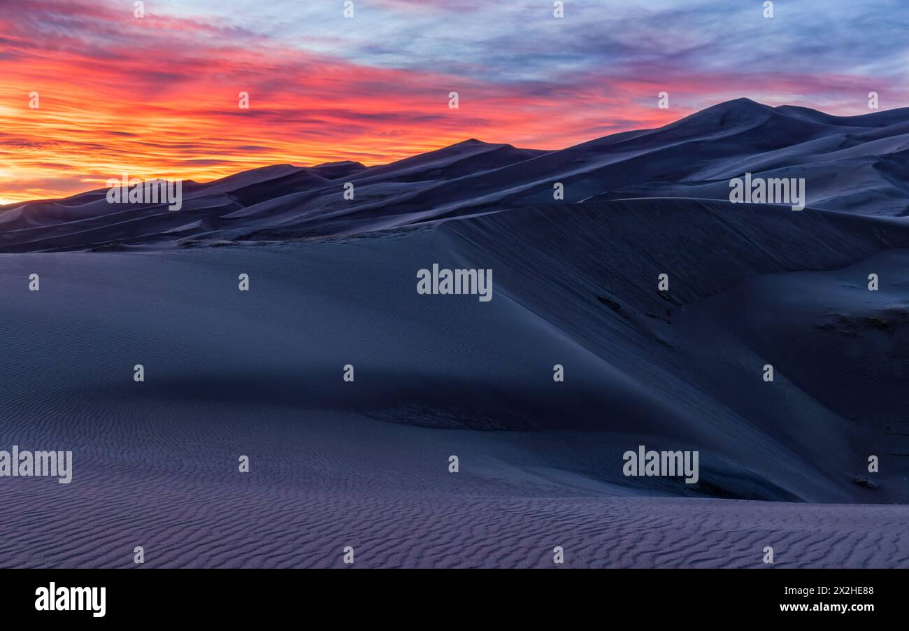 A red, orange and yellow sunset sky above a blue and purple dunefield ...