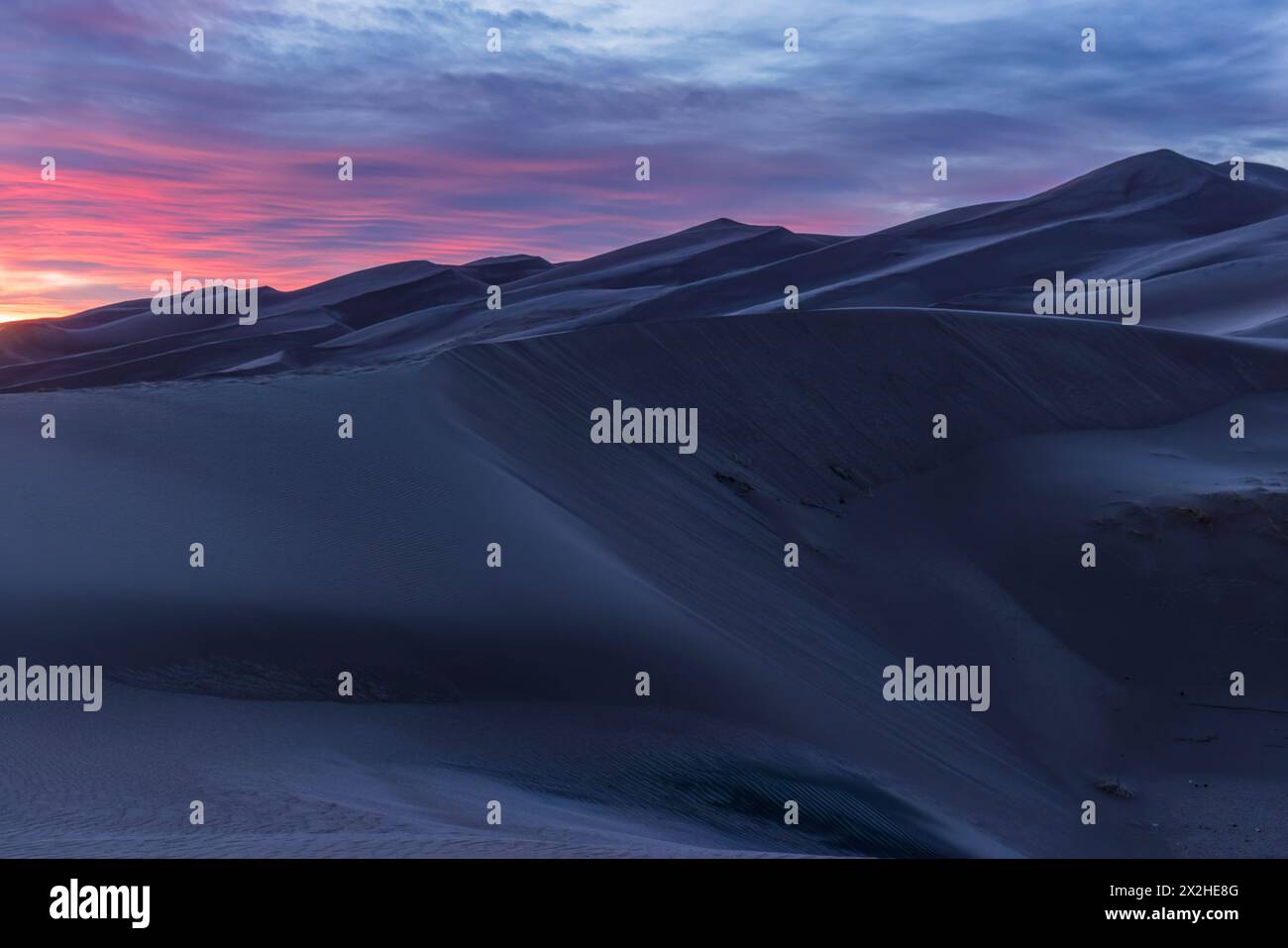 A colorful twilight sky above a blue and purple dunefield in Great Sand ...