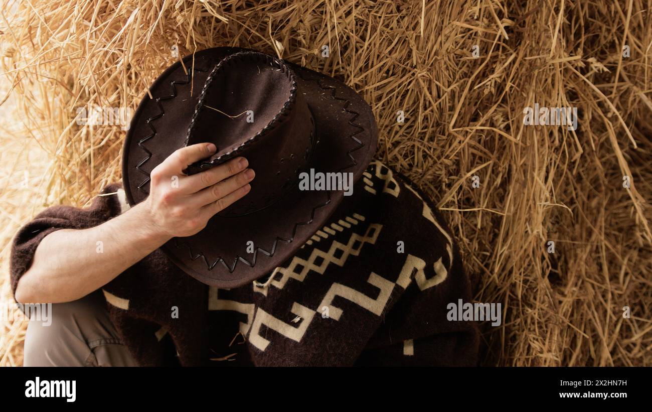 Tired cowboy leaning on hay bale Stock Photo - Alamy