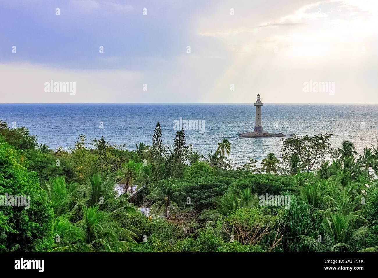 View of a lighthouse in the sea near a rocky shore with palm trees ...