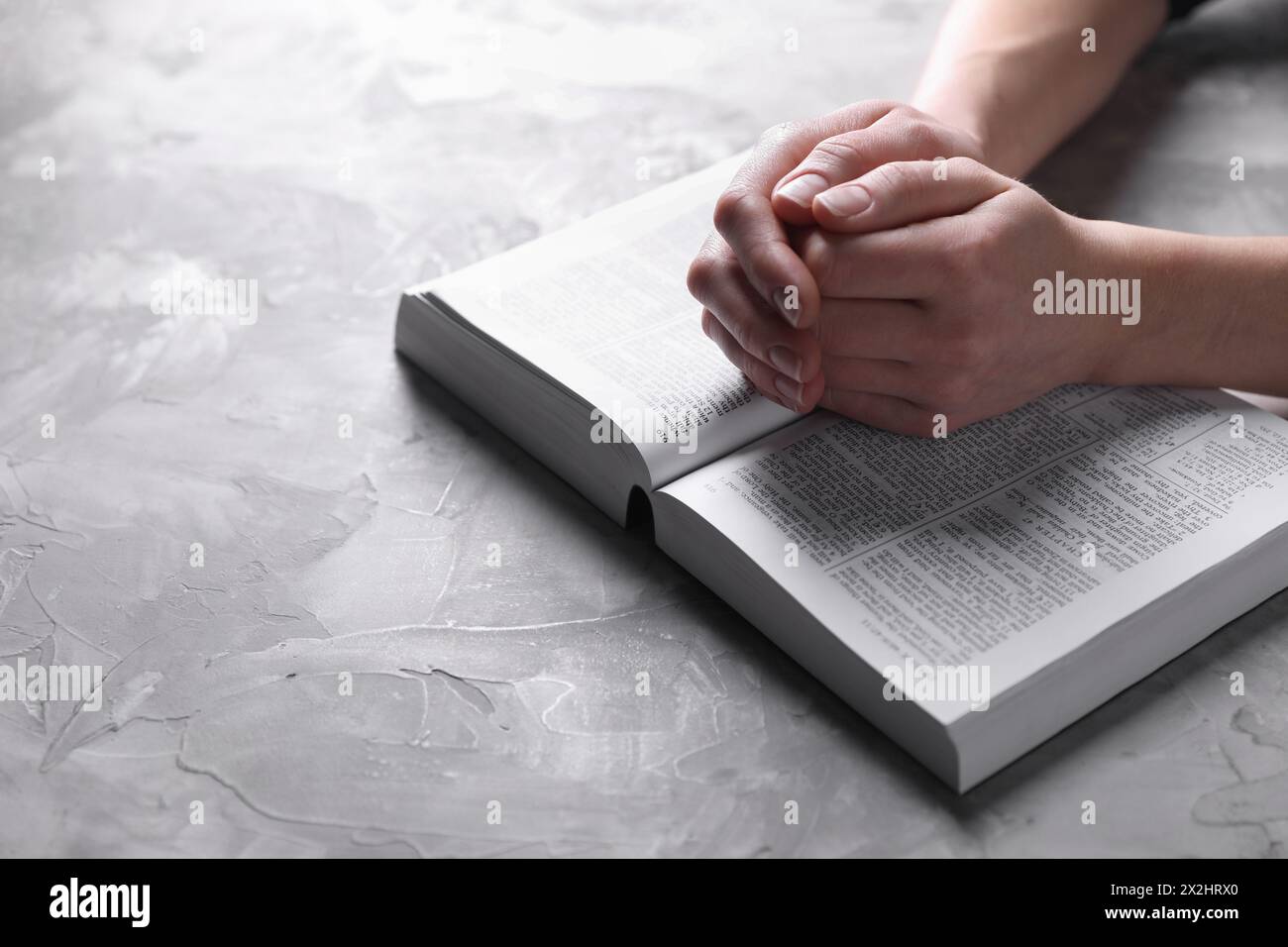Religion. Christian woman praying over Bible at gray textured table ...