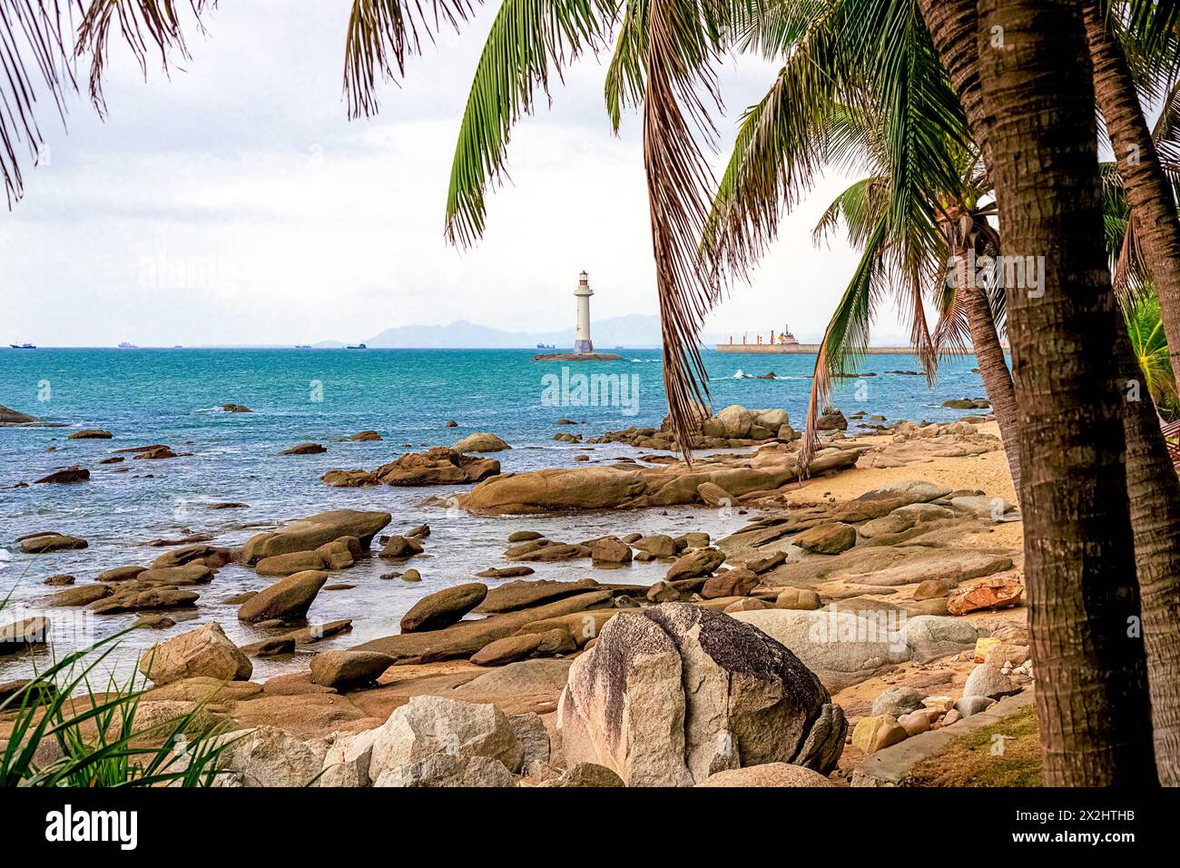 View of a lighthouse in the sea near a rocky shore with palm trees ...