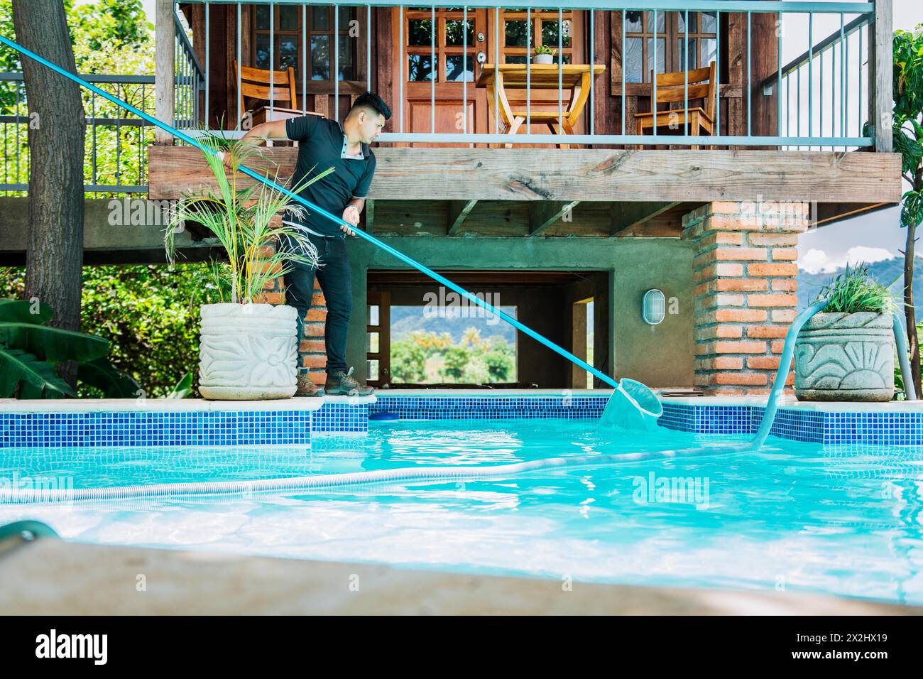 Man cleaning swimming pool water with a skimmer. Maintenance person ...