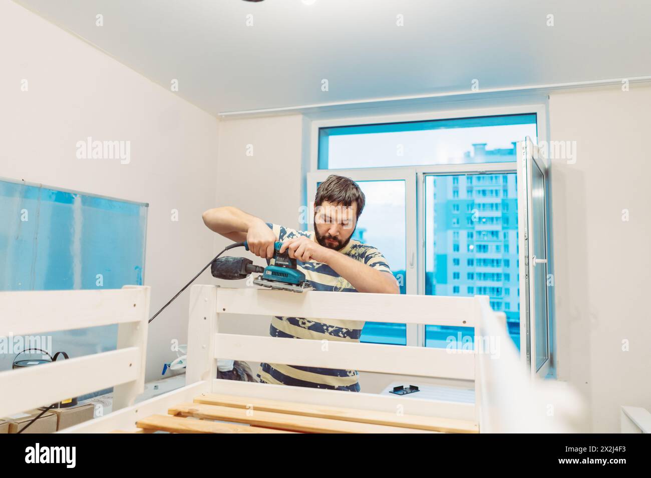 man rubs wooden child bed with power sander or grinder removing old ...