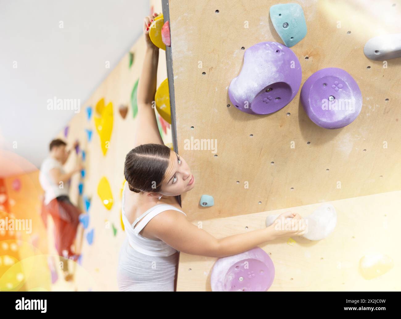 Europian girl client of gym trains doing exercises on artificial wall ...