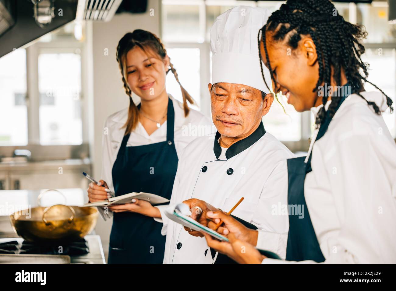 Senior Asian chef in a restaurant kitchen educates multiracial students ...
