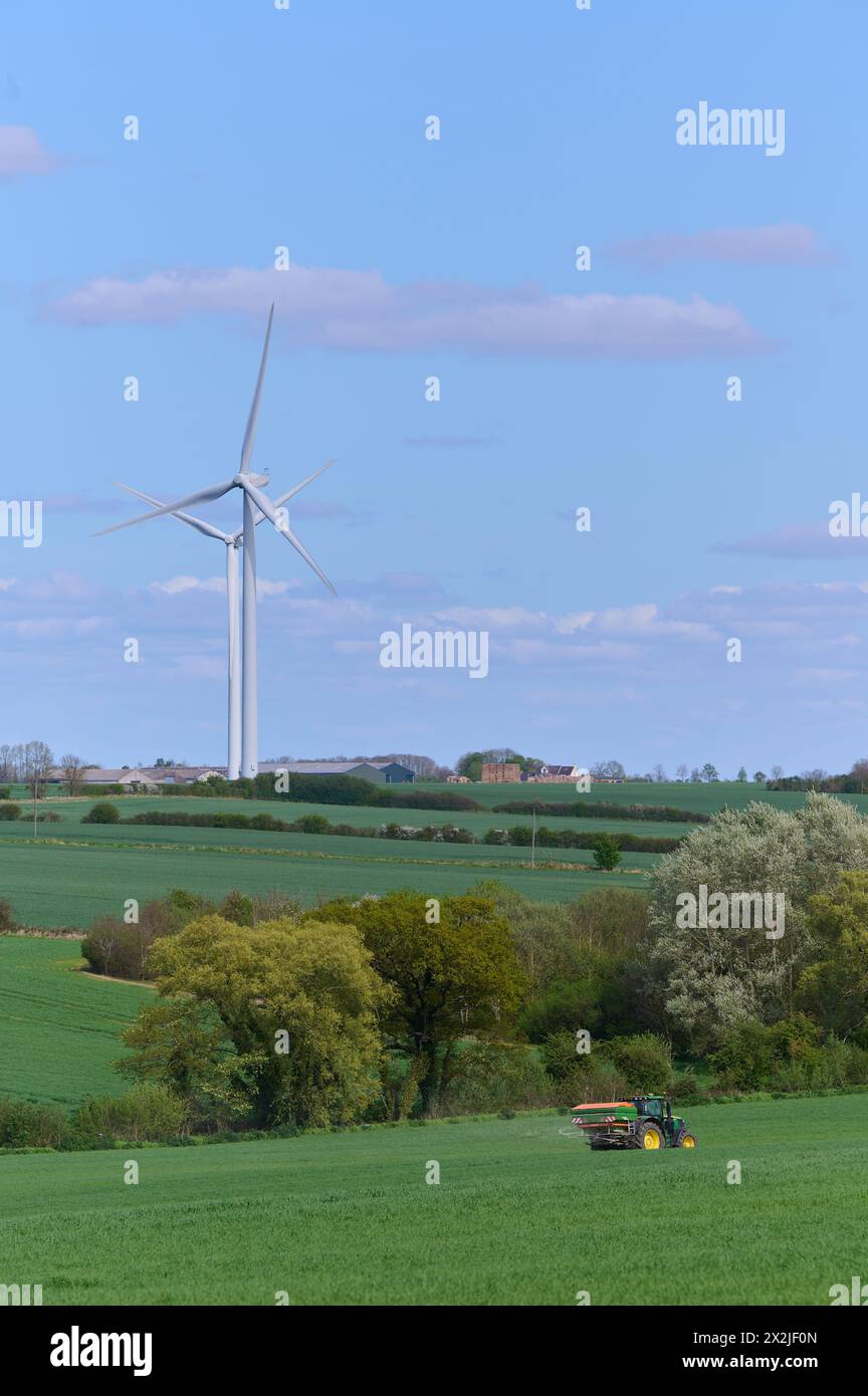 Two wind turbines over English countryside and a tractor against blue ...
