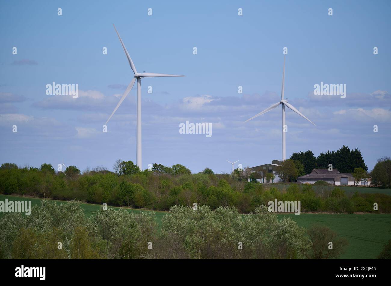 Two wind turbines over English countryside against blue sky with small ...