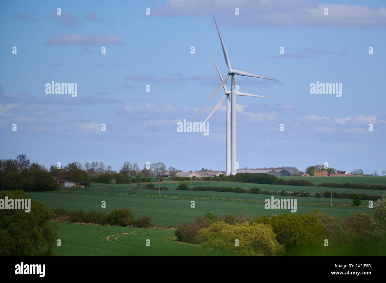Two wind turbines over English countryside against blue sky with small ...