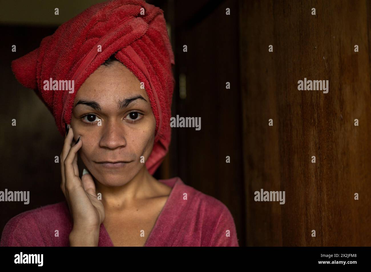 Young transgender man (26) with bathrobe and towel covering his head ...