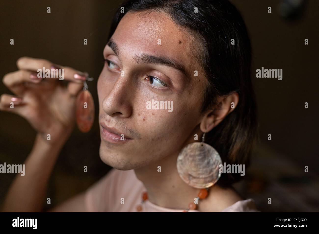 Young transgender man (22) is in his room putting on his accessories ...