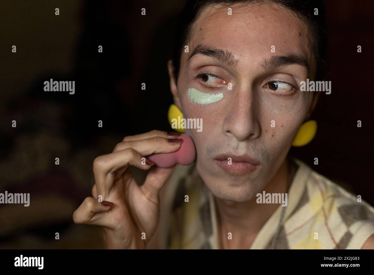 A transgender young man (22) is in his room putting on makeup. Concept ...